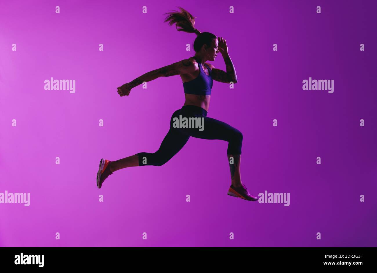 Female sprinter running on purple background. Portrait of woman with ...