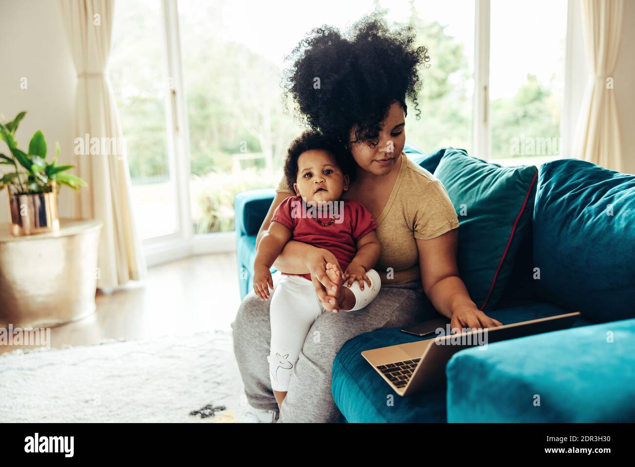 African american woman baby sitting on sofa using laptop. Freelancer ...