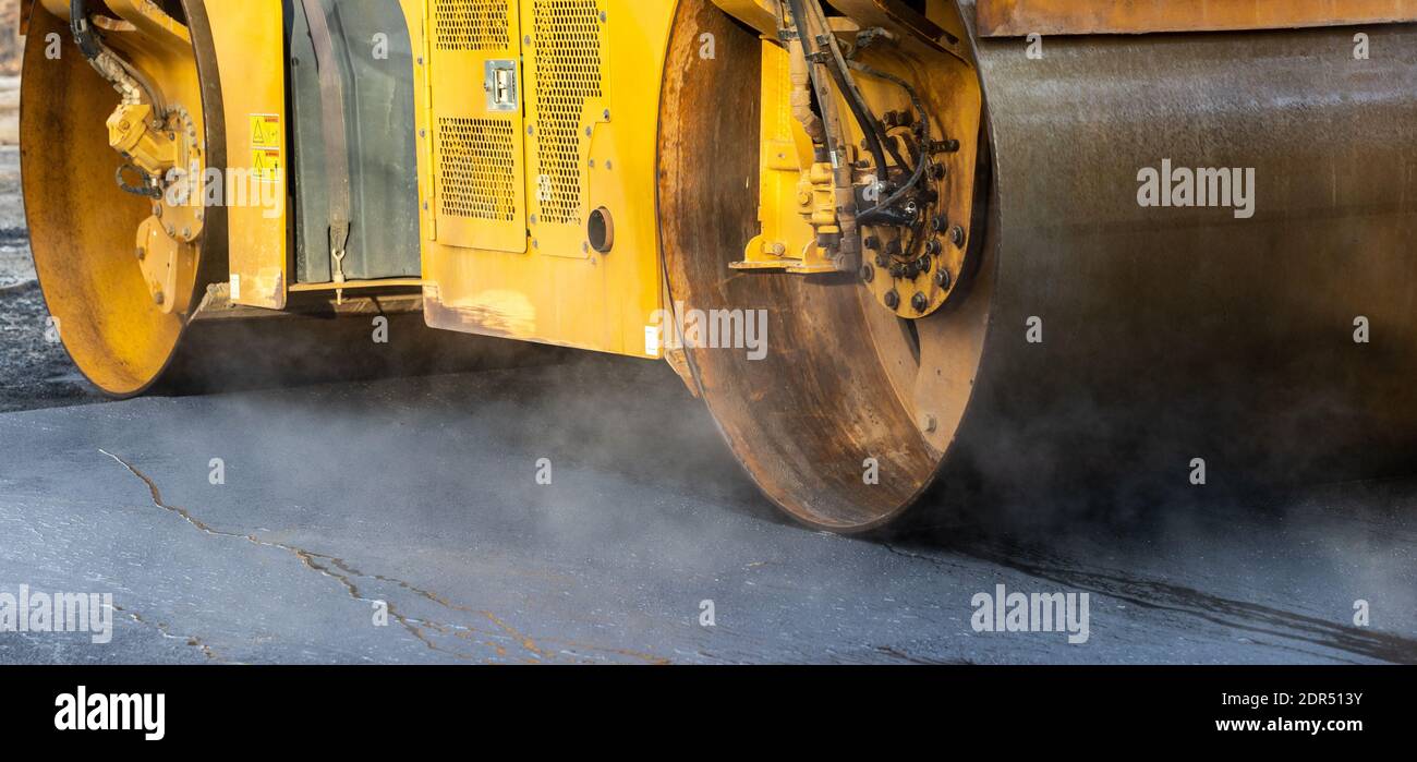 Steam billows up from hot asphalt being rolled during road paving work ...