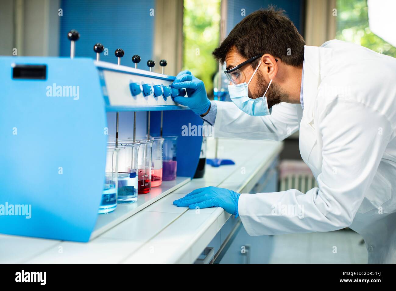 Young researcher with protective goggles checking test tubes in ...