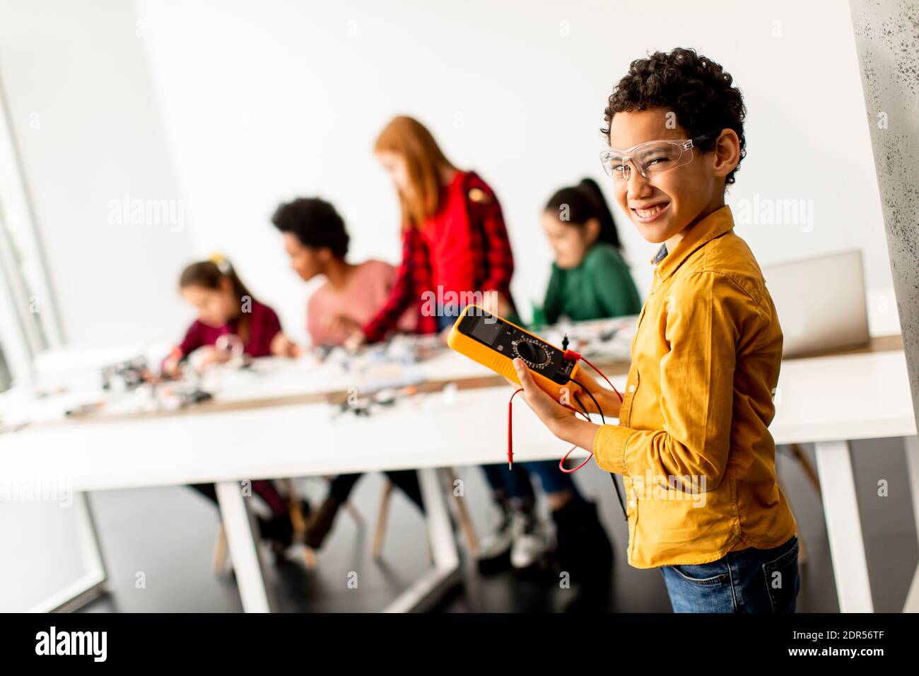 Cute little boy standing in front of group of kids programming electric ...