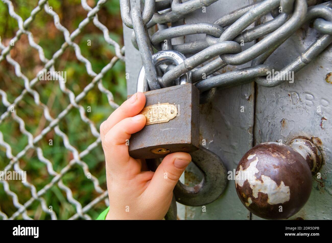 Padlock with chain and hand of a child on iron gate Stock Photo - Alamy