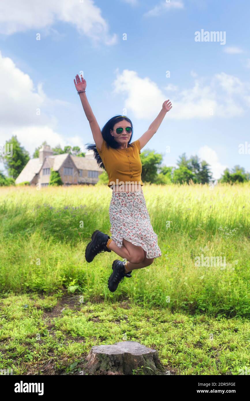 A chinese woman jumping off of a tree stump with tall grass and a ...