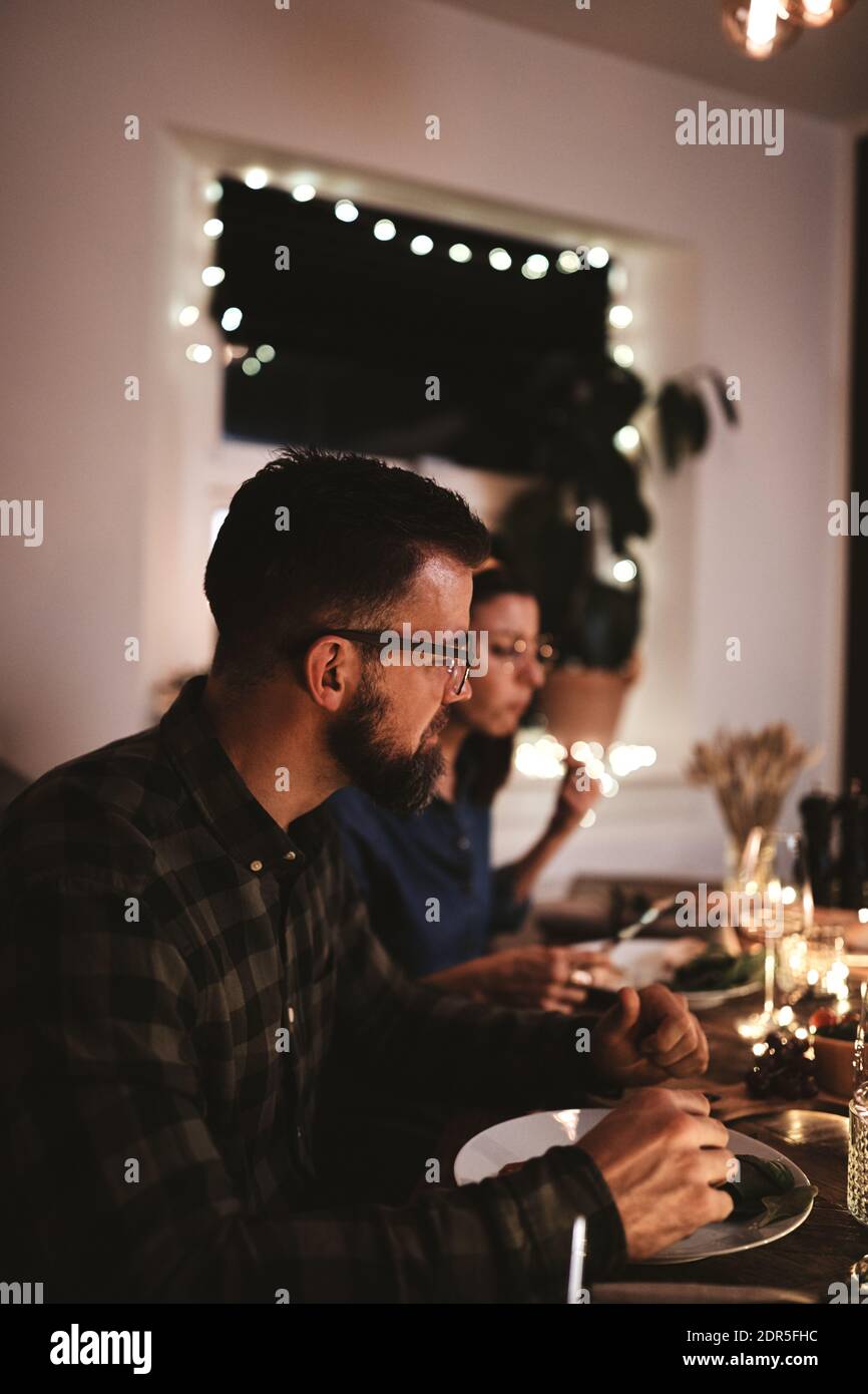 Smiling man having dinner with friends while sitting around a candlelit ...