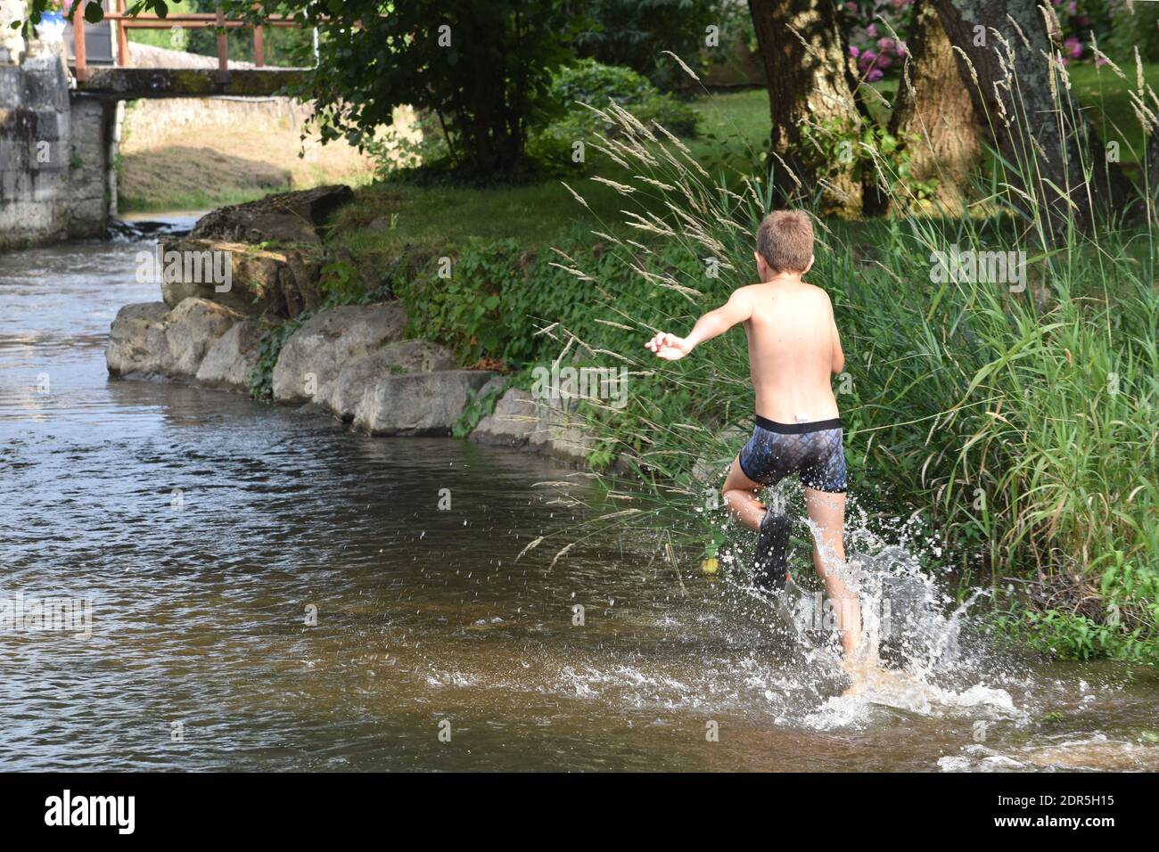 Boy running through shallow water on summer day, river Yonne, Nièvre ...