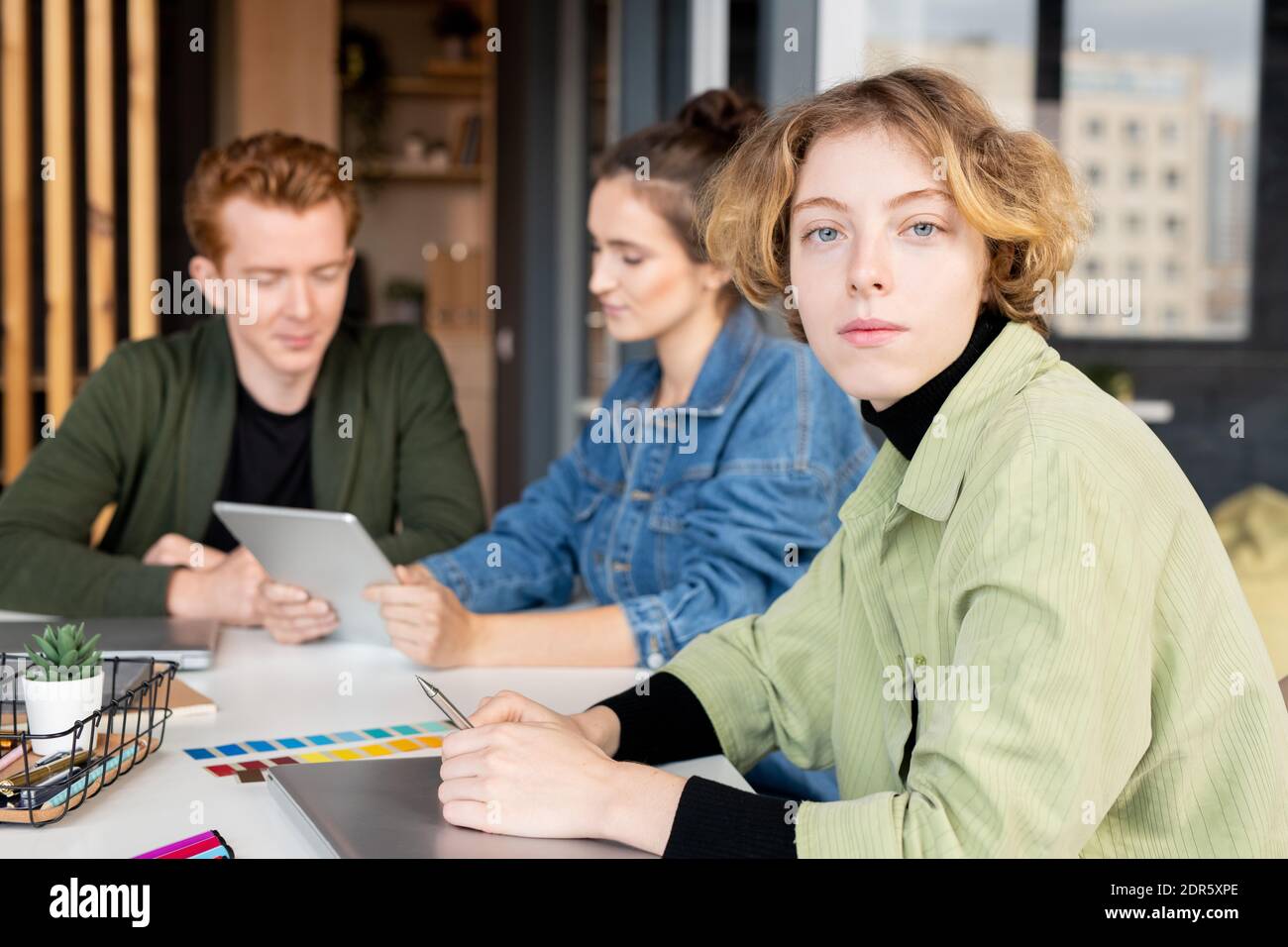 Young blond serious female mobile app developer looking at you while ...