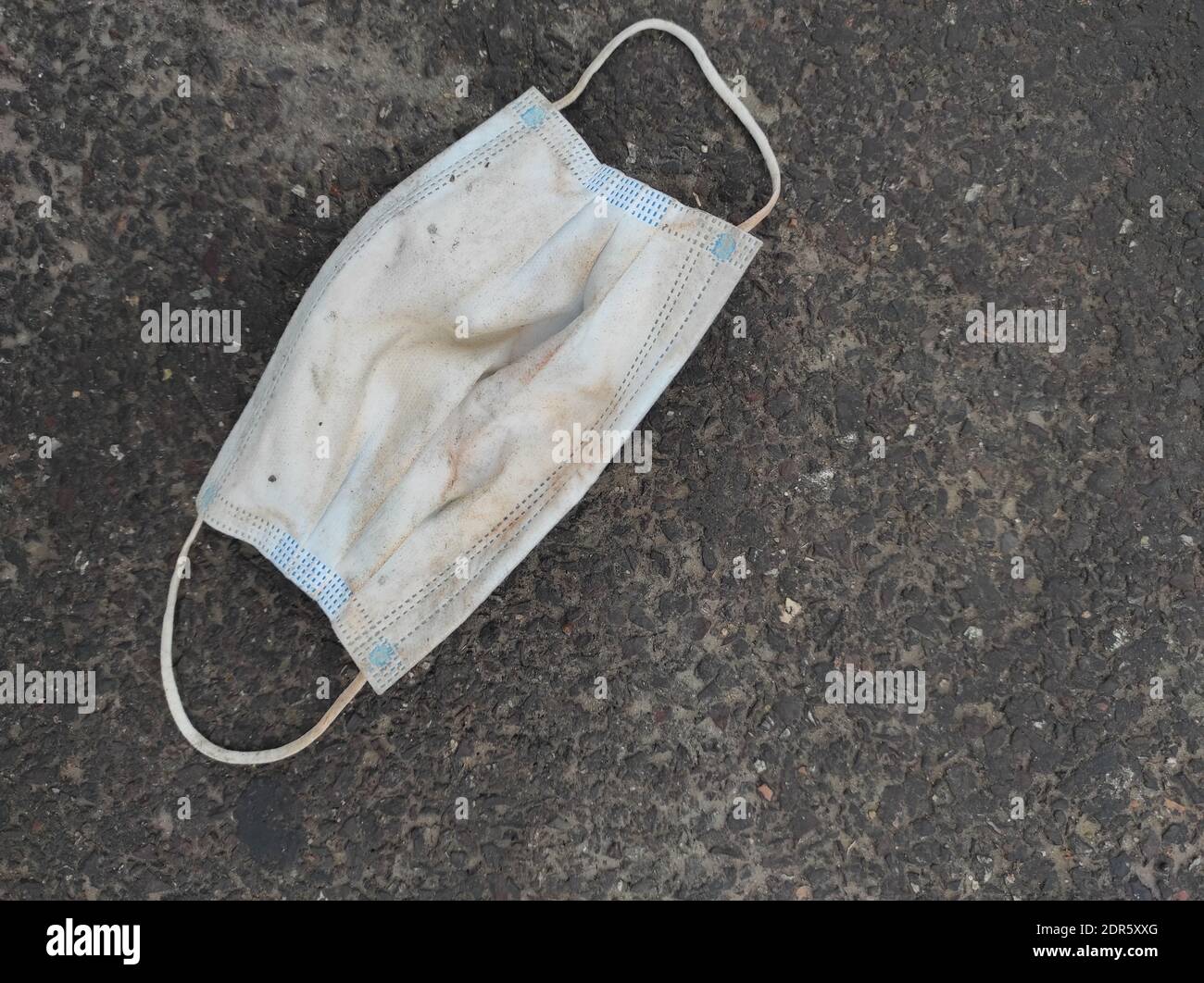 A top view of a dirty used facemask on the ground - concept of COVID-19 ...