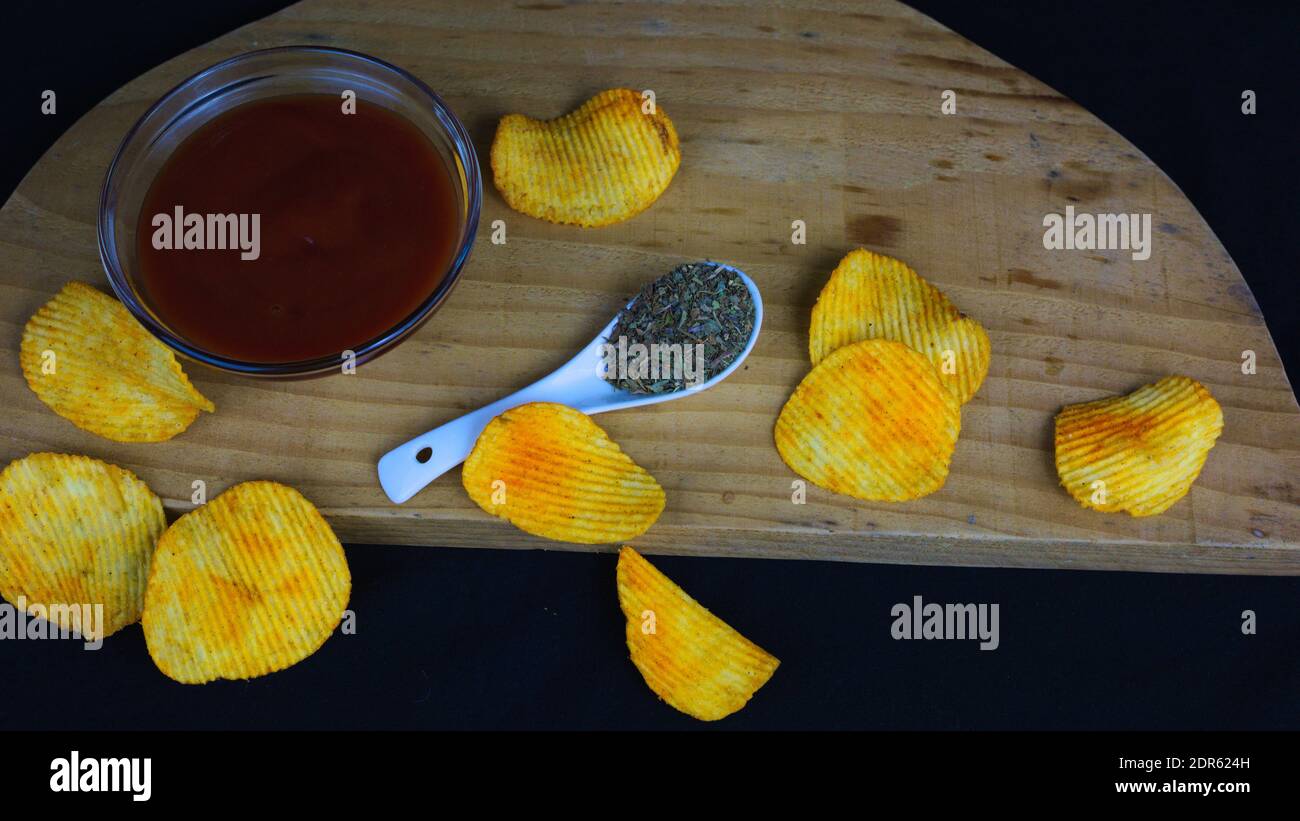 A high angle shot of potato chips, ketchup and seasonings on a chopping ...
