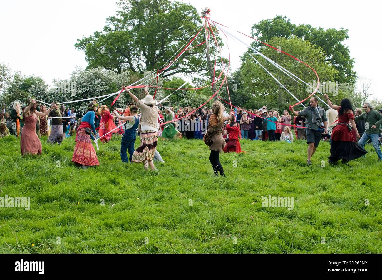Revellers Dressed In Costume Dance Around The Maypole In A Field At The ...