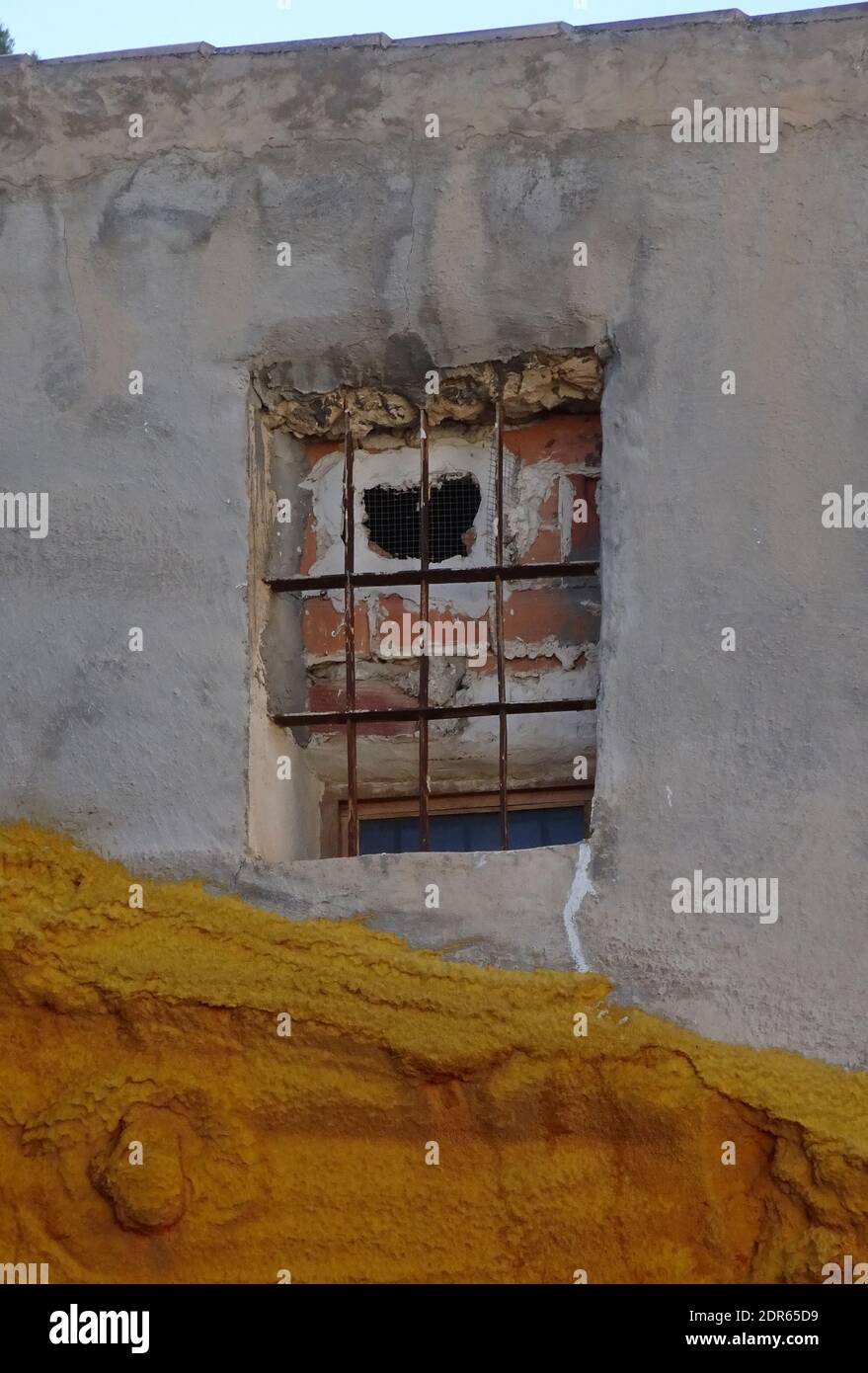 An old white and yellow painted wall and a partly bricked-up window ...