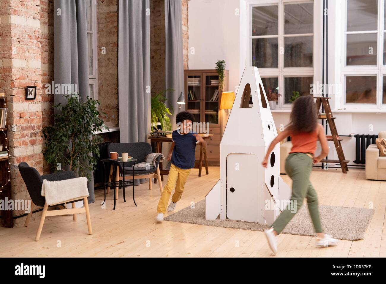 Two joyful siblings running after each other and around big white ...