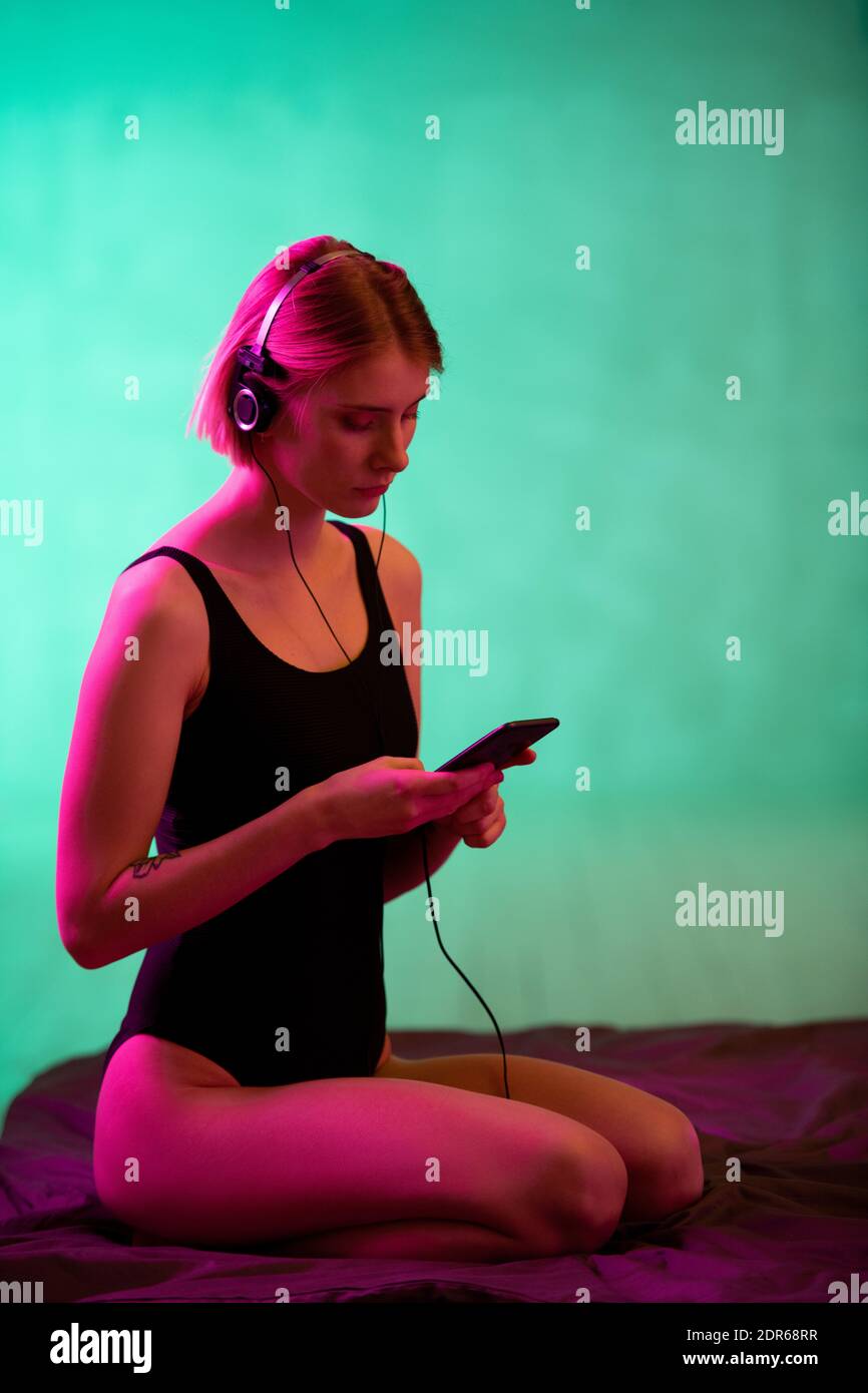 Pretty girl in headphones and black leotard scrolling through playlist ...