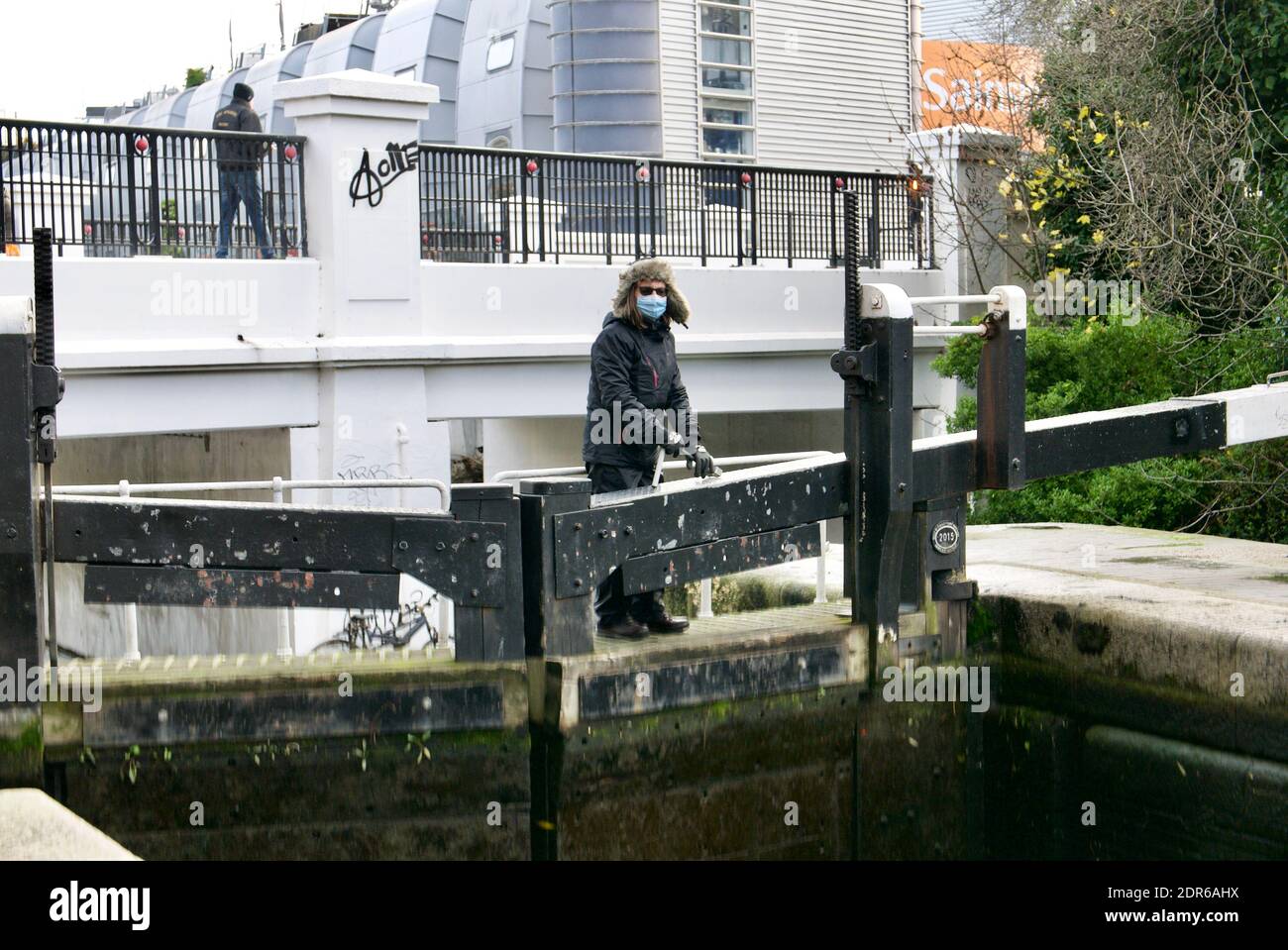 Elderly woman wearing a facemask and winter clothing opens the canal ...