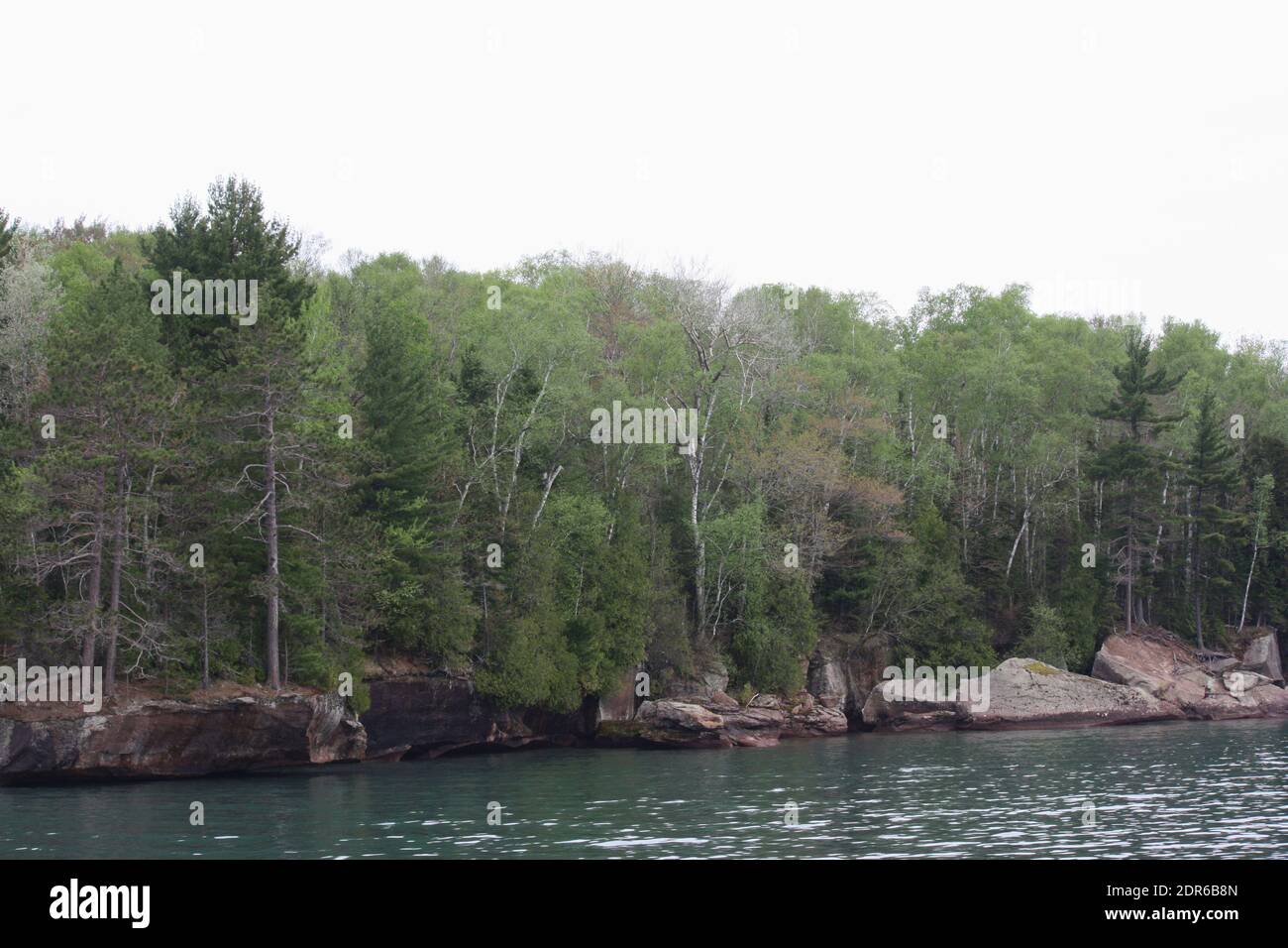 The rocky shoreline of Lake Superior lined with a variety of trees ...