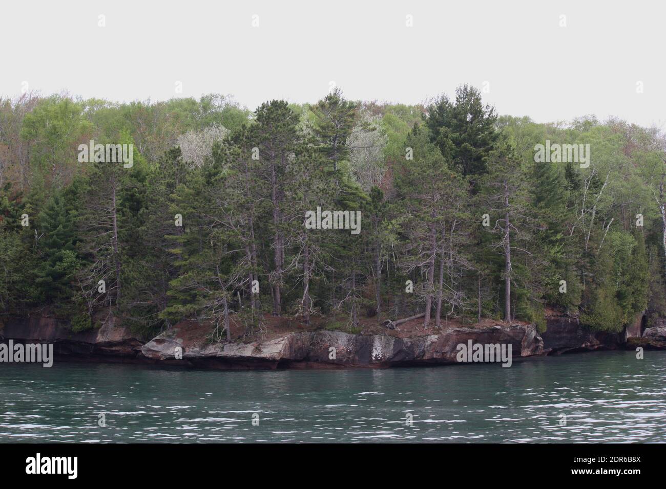 The rocky shoreline of Lake Superior lined with a variety of trees ...