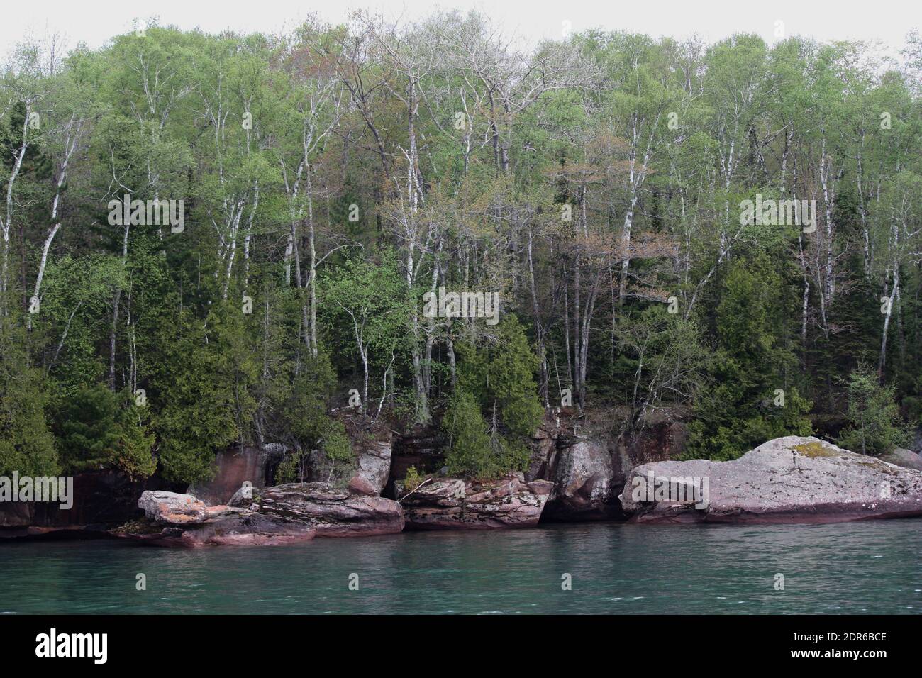 The rocky shoreline of Lake Superior lined with a variety of trees ...