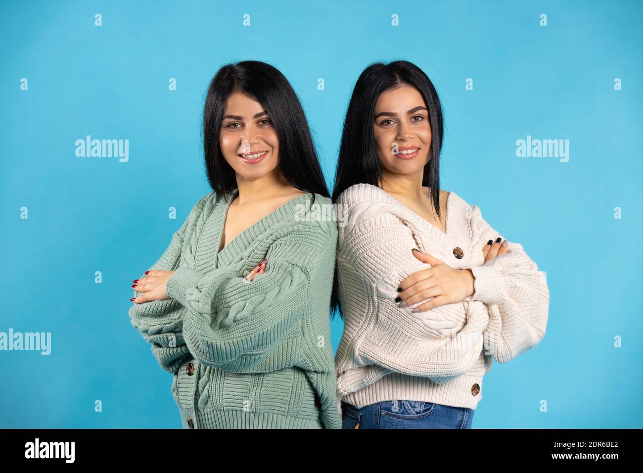 Twin girls in identical clothes on a blue background, braided their ...