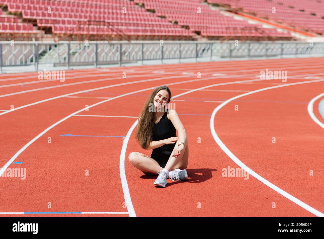 A female coach with dark hair stands on the red running track of the ...
