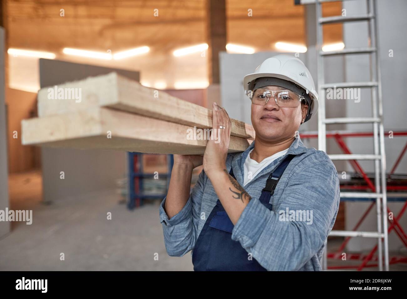 Waist up portrait of smiling female worker carrying wood boards while ...