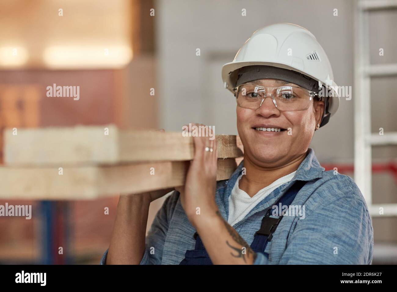 Front view portrait of smiling female worker carrying wood boards while ...