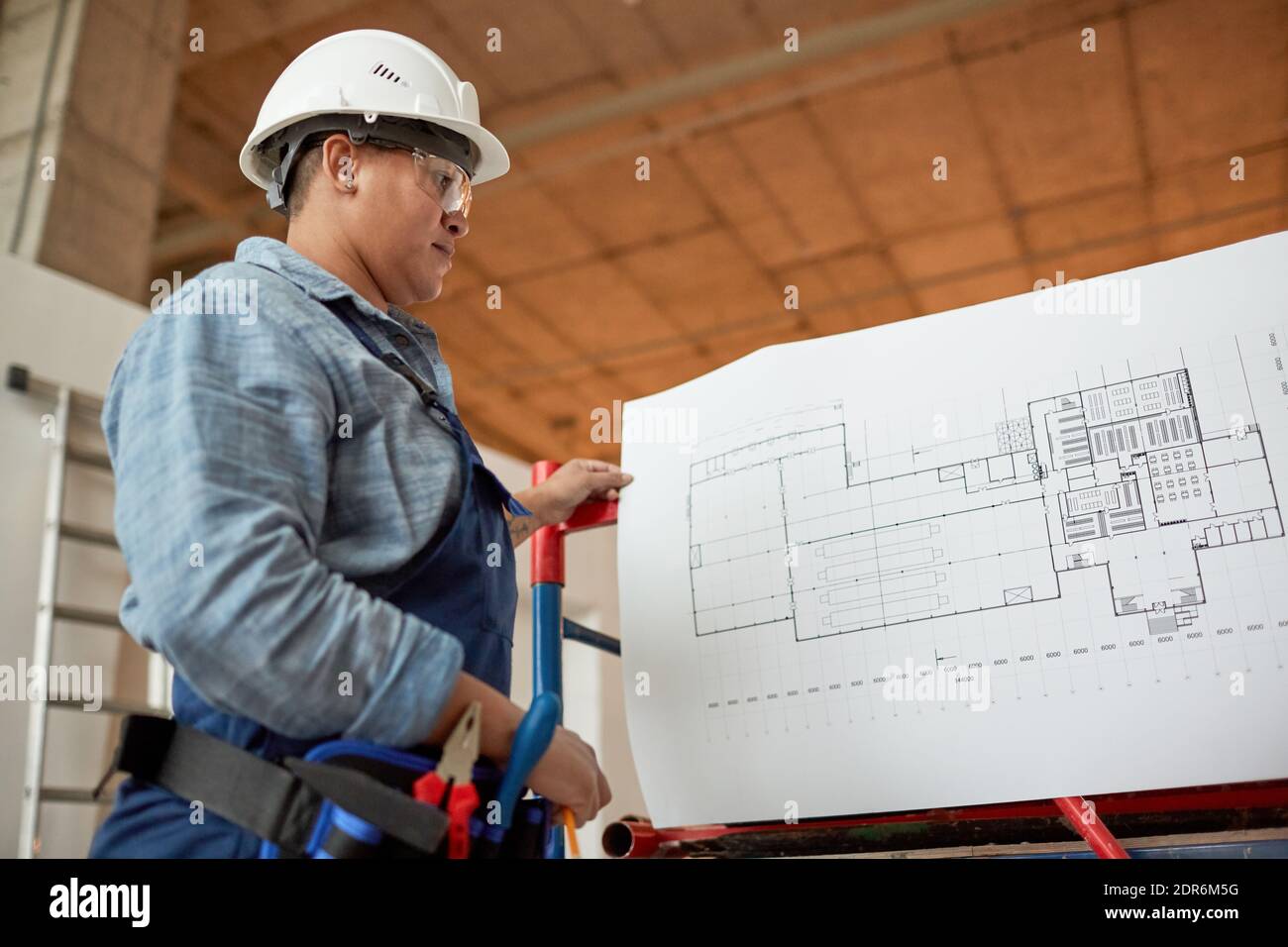 Low angle portrait of female engineer inspecting floor plans while ...