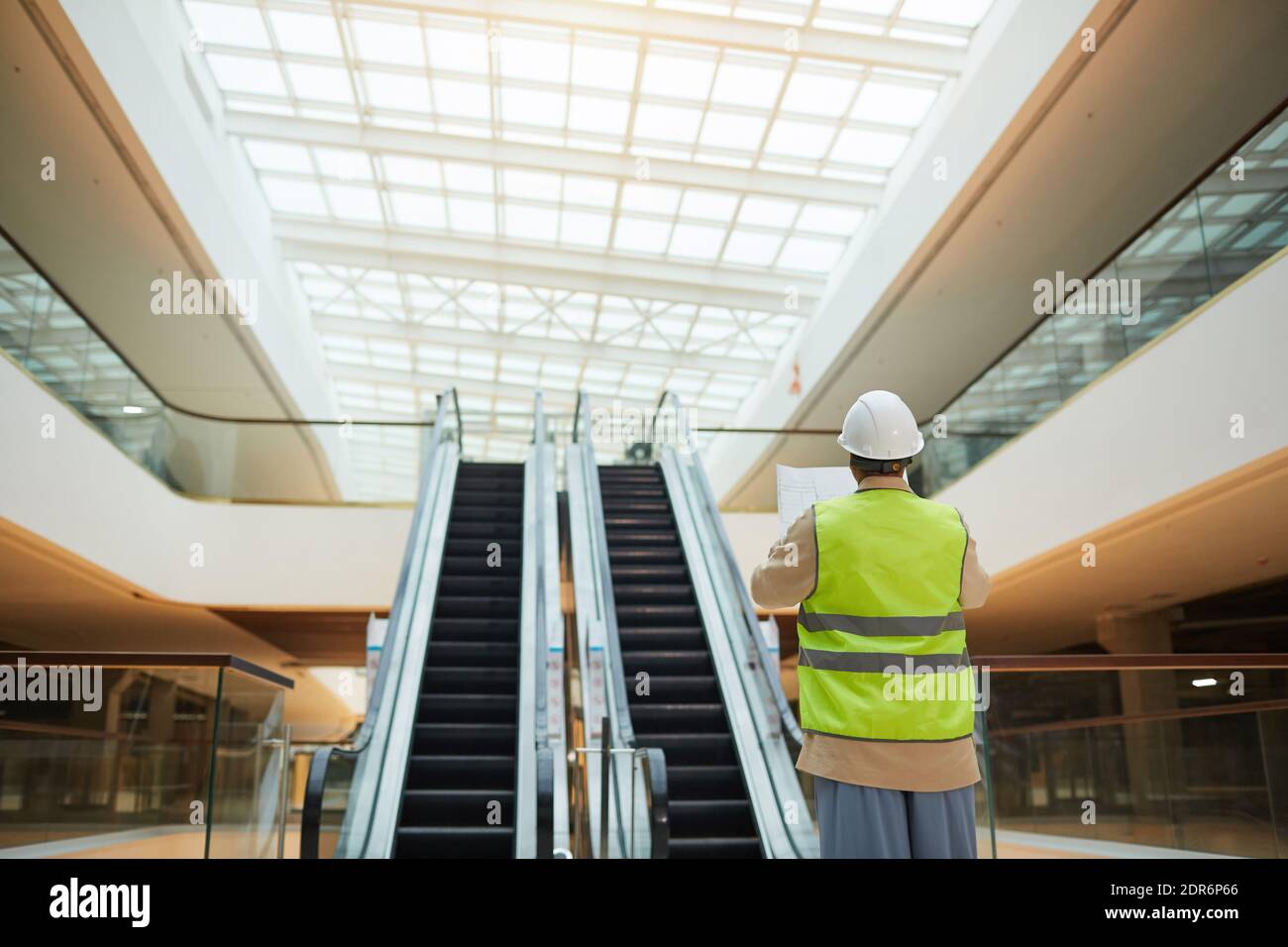 Back view portrait of female engineer holding blueprints while standing ...