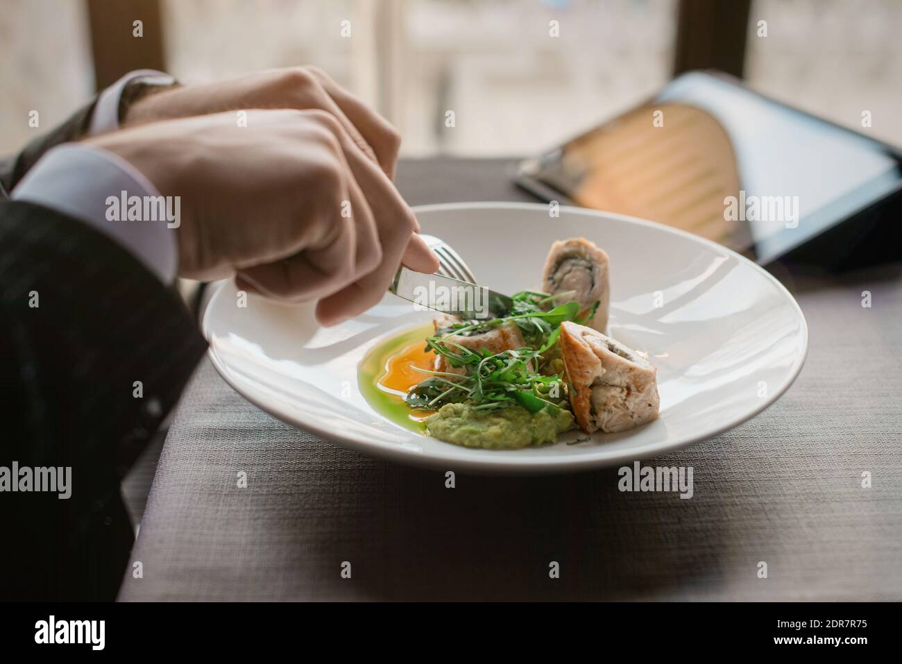 A young and attractive man uses his tablet while eating turkey fillet ...