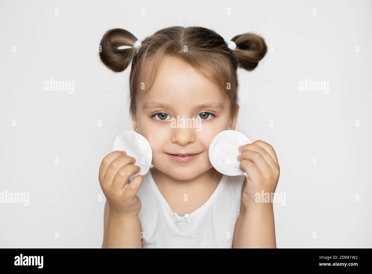 Studio shot of pretty kid girl, cleansing her face by cotton pads ...