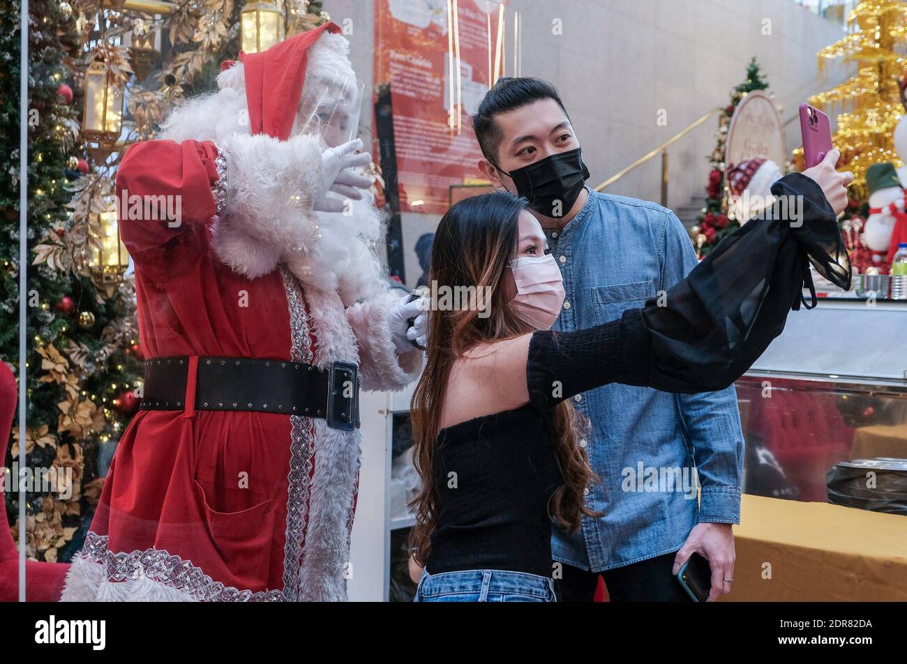 A couple wearing face masks takes a selfie with a Santa Claus at ...