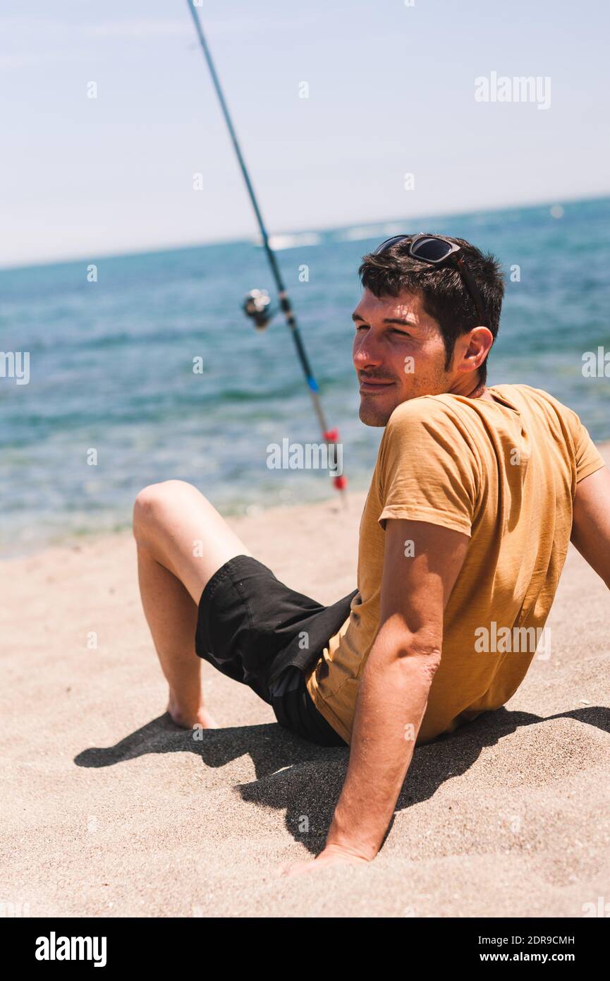 Man Sitting With Fishing Rod At Beach Stock Photo - Alamy