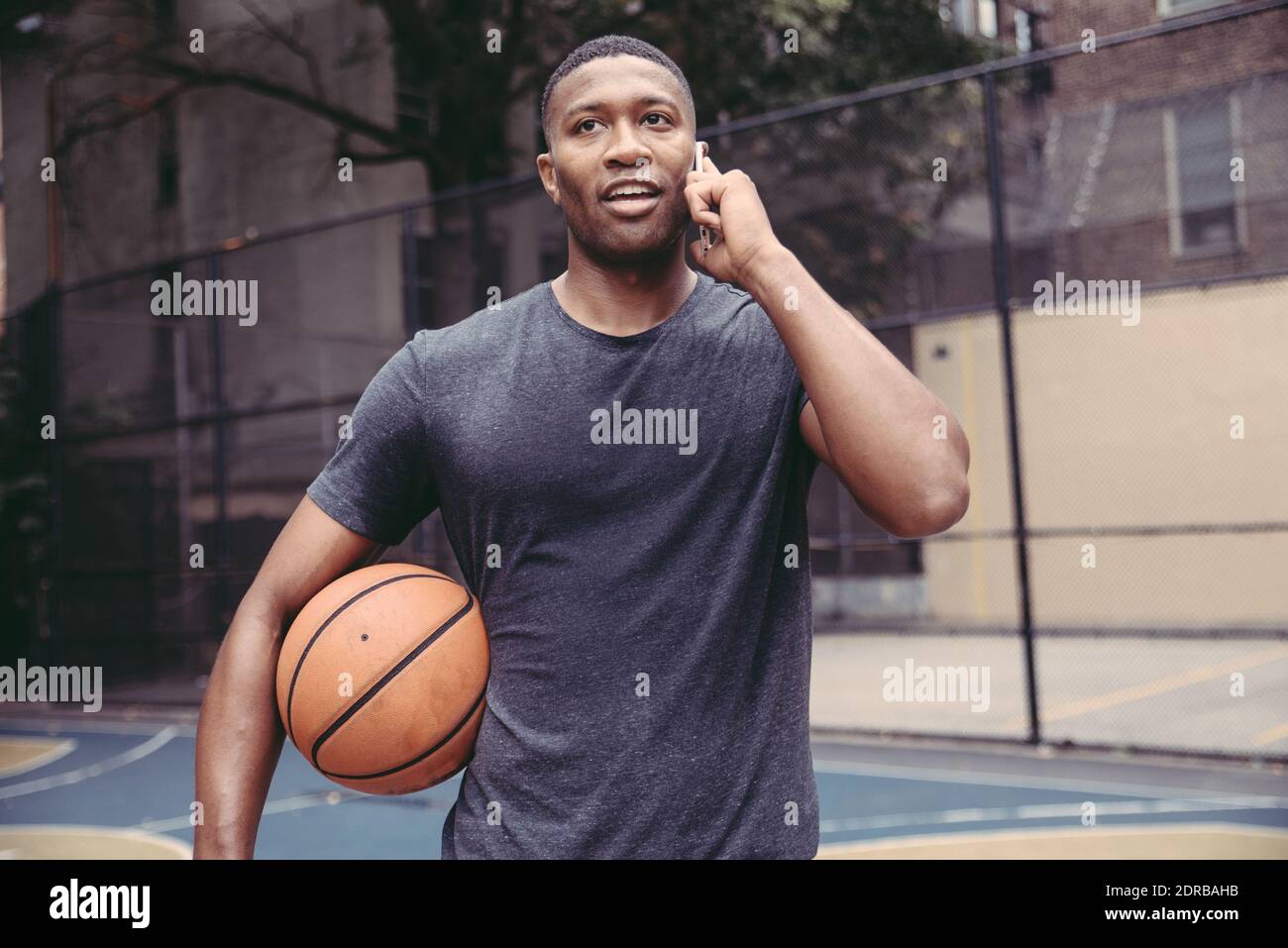 Young Man Talking On Mobile Phone While Standing In Basketball Court ...
