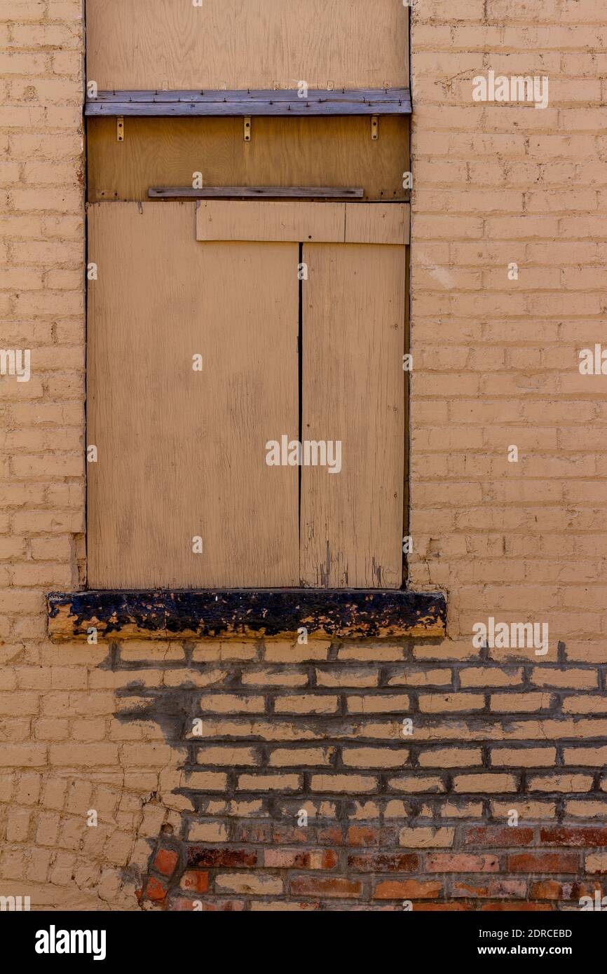 Texture background of a rugged old exterior beige painted exterior brick wall with a boarded up ...