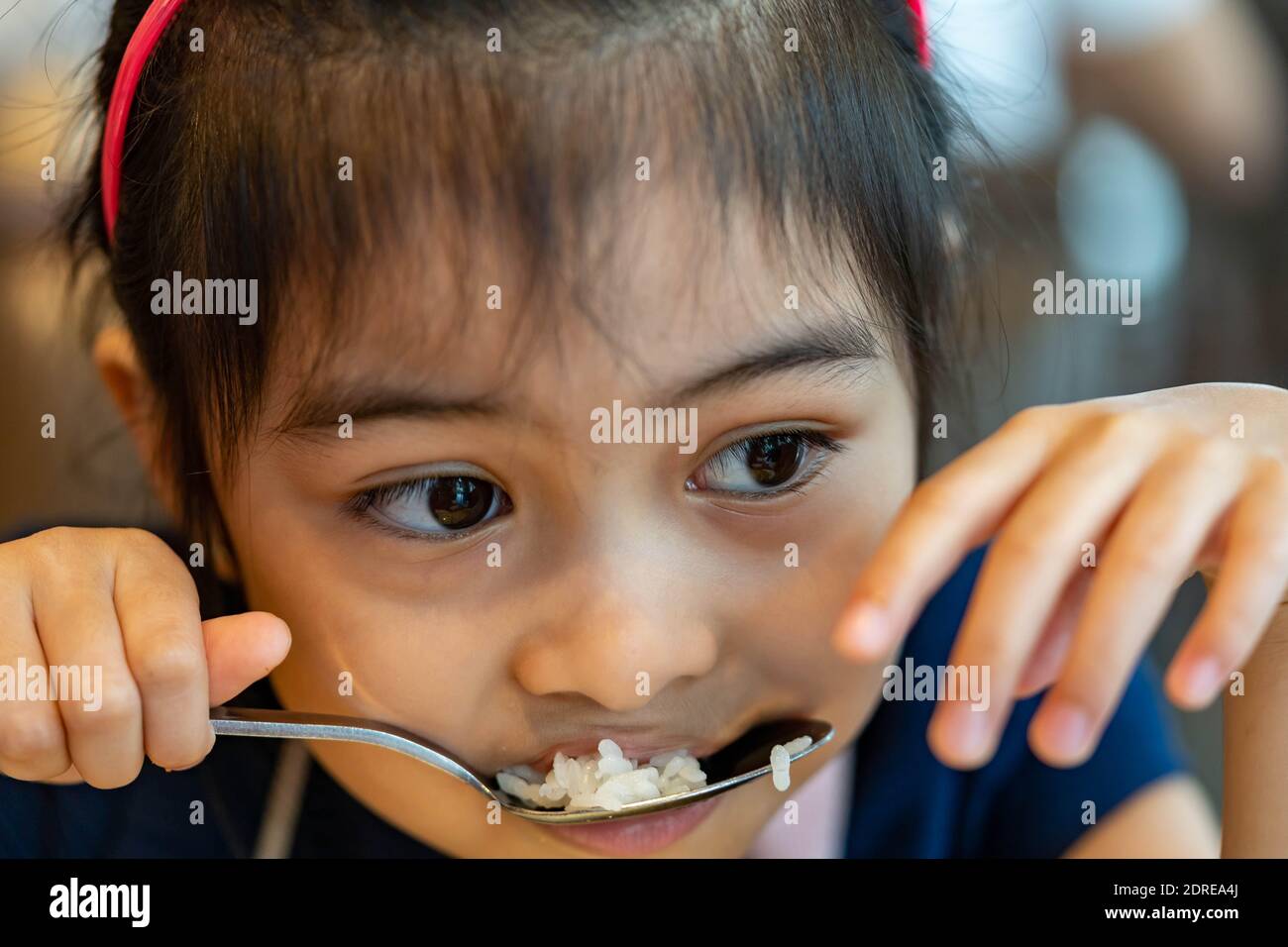 Female asian child while eating rice using spoon. Child enjoys eating ...