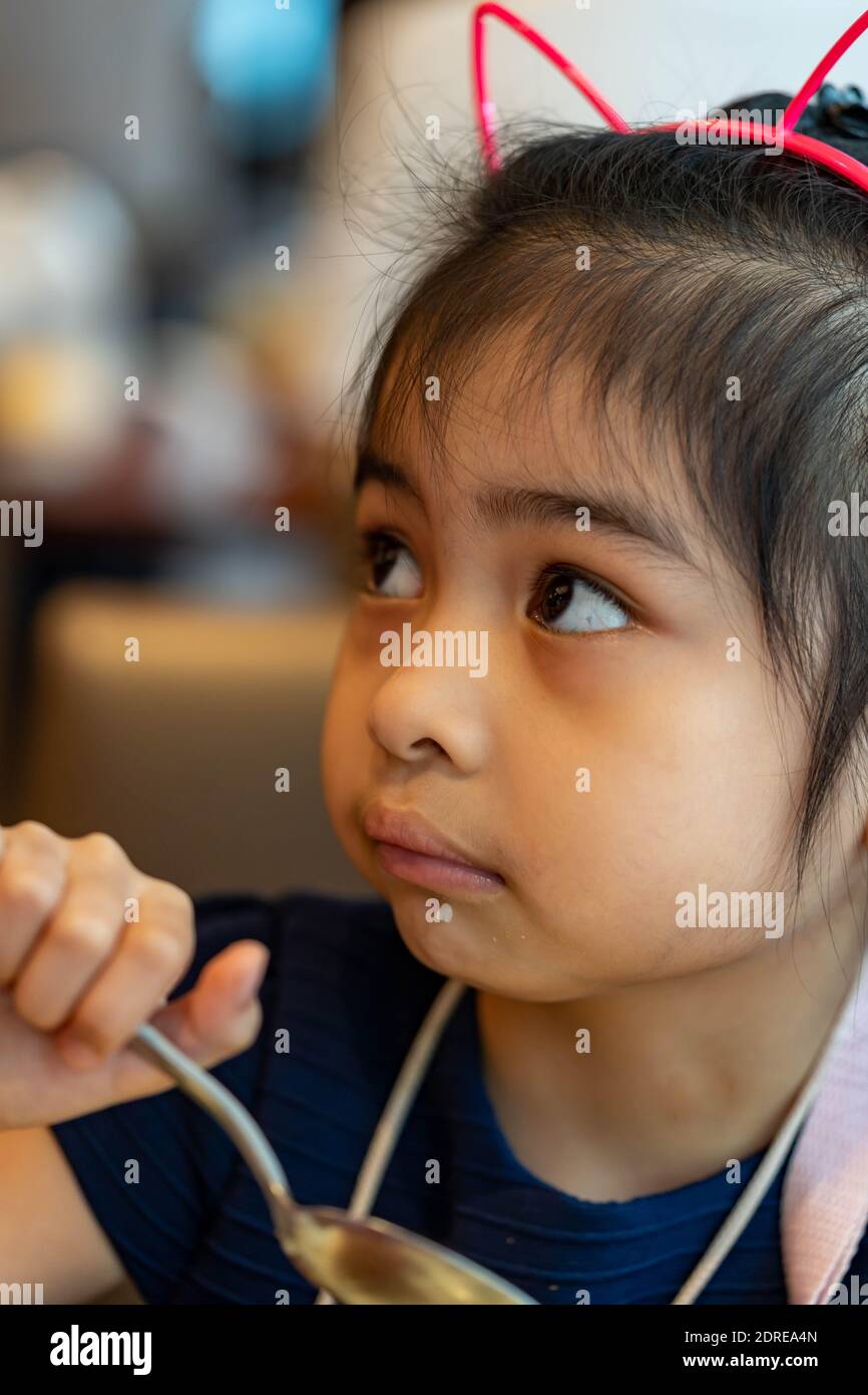 Female asian child while eating rice using spoon. Child enjoys eating ...