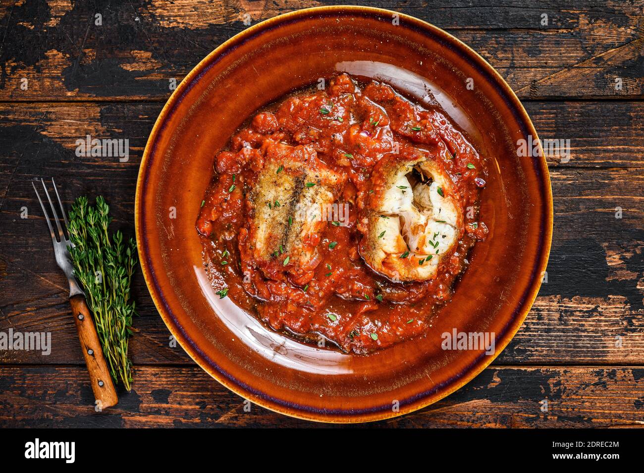 Roast grenadier white fish fillet with tomato sauce in a plate. Dark ...