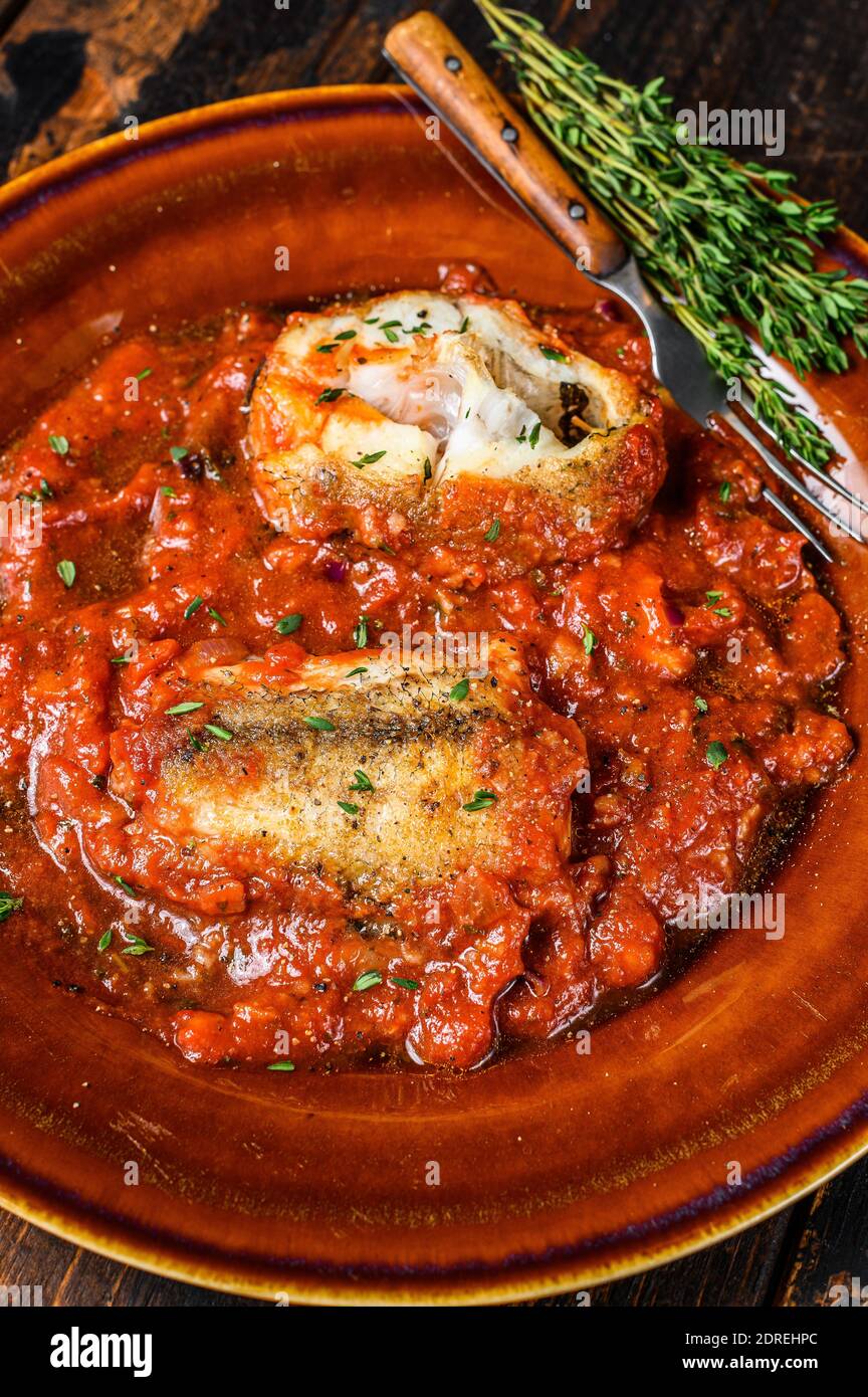 Roast hake white fish fillet with tomato sauce in a plate. Dark ...
