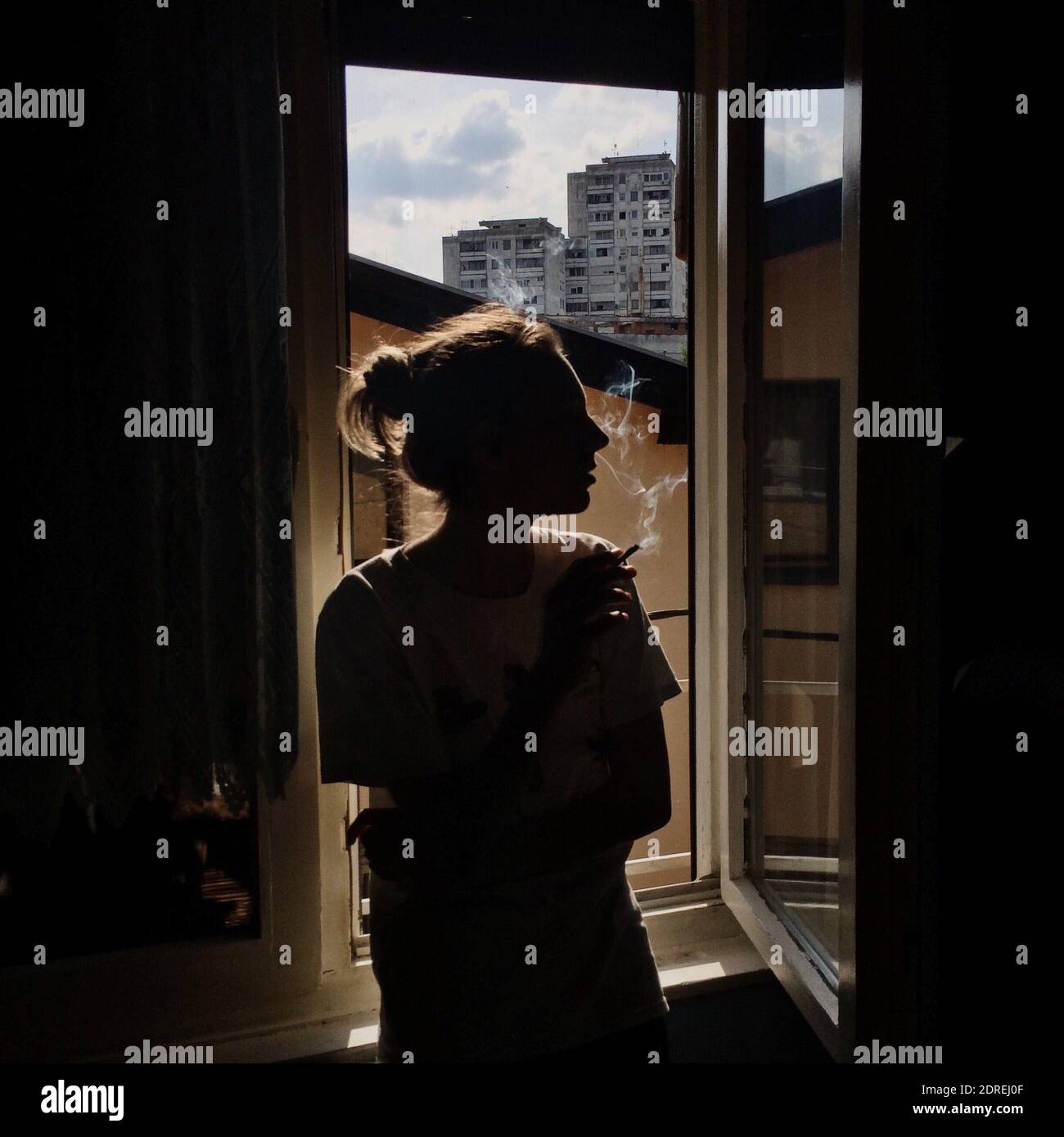 Young woman standing window smoking hi-res stock photography and images ...