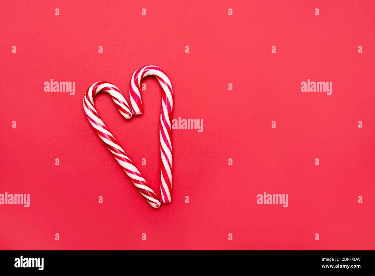 Two candy canes together create a heart shape on red background with a ...