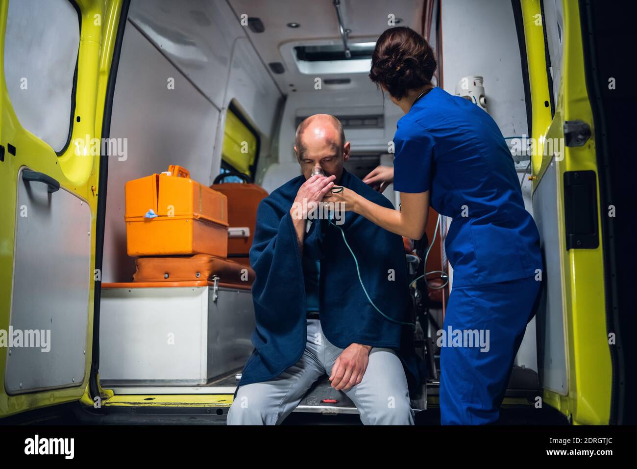 A paramedic gives an oxygen mask to an injured man sitting in an ...