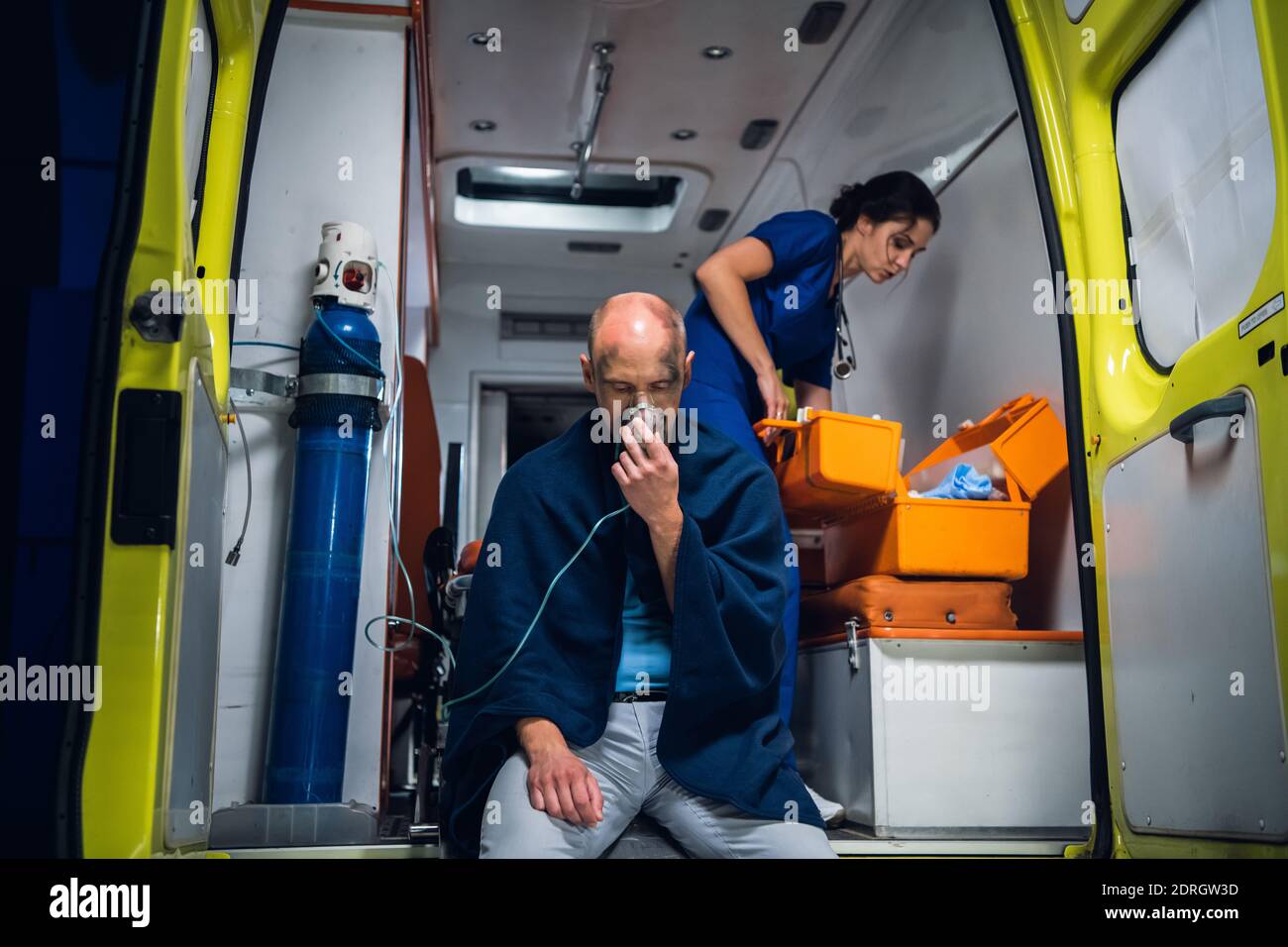 Man Sits With Oxygen Mask Nurse In Uniform Packs Equipment In Medical