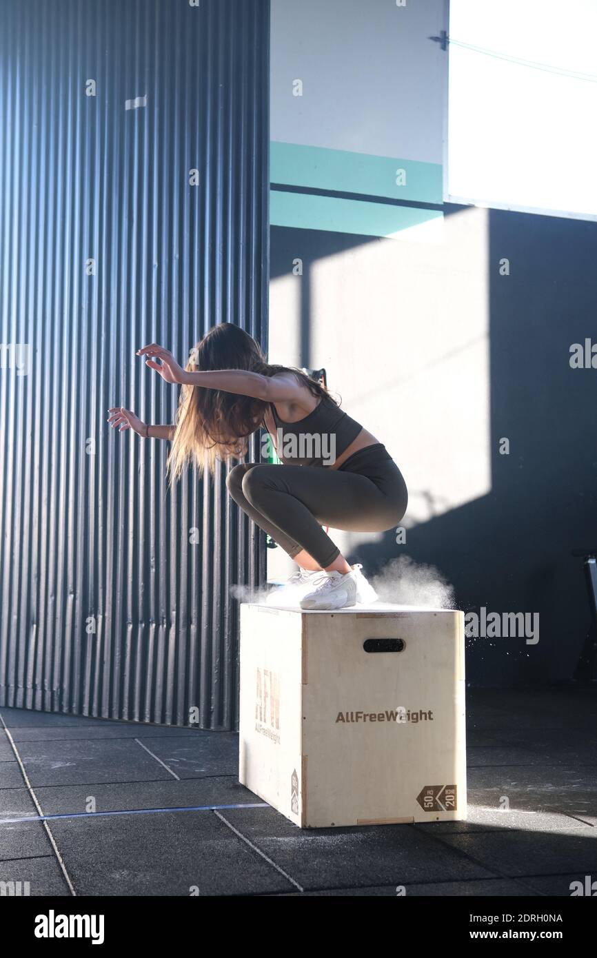 Fit young woman box jumping at a crossfit style on gray background ...