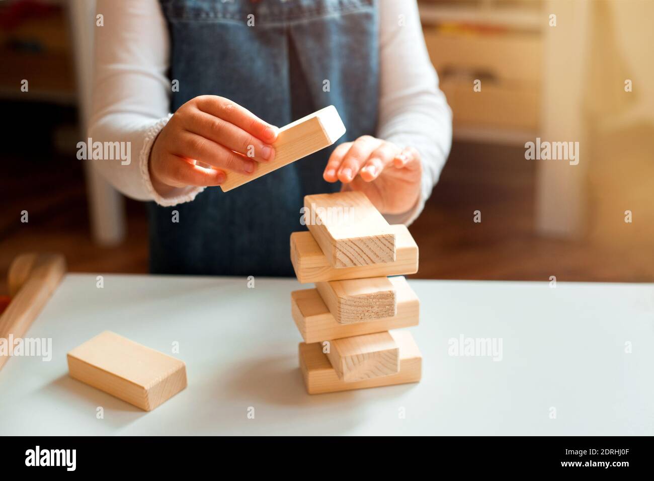 Little girl playing with wooden bricks at home. She builds little tower ...