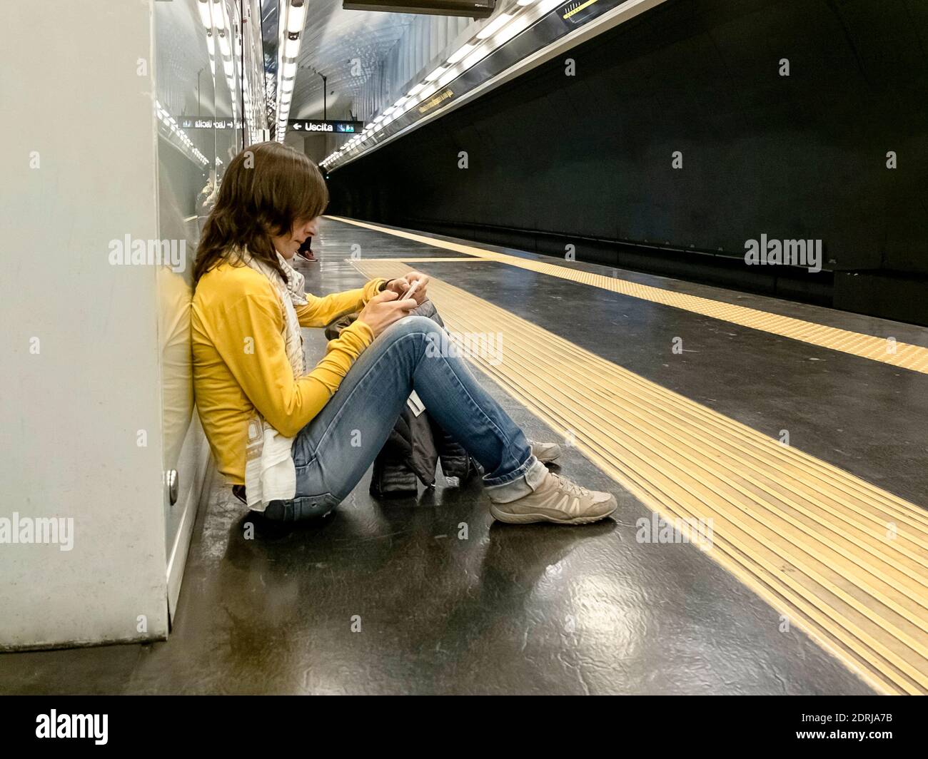 Young woman sitting on ground using phone while leaning on underground ...