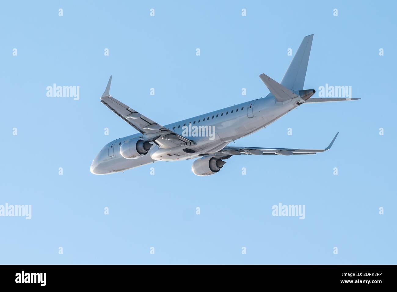 Modern white passenger aircraft flies in the air on a clear sunny day ...