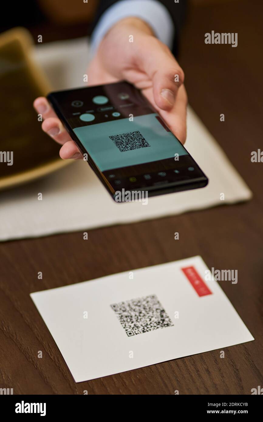 Cropped photo of hand with smartphone scanning a QR-code on a ...