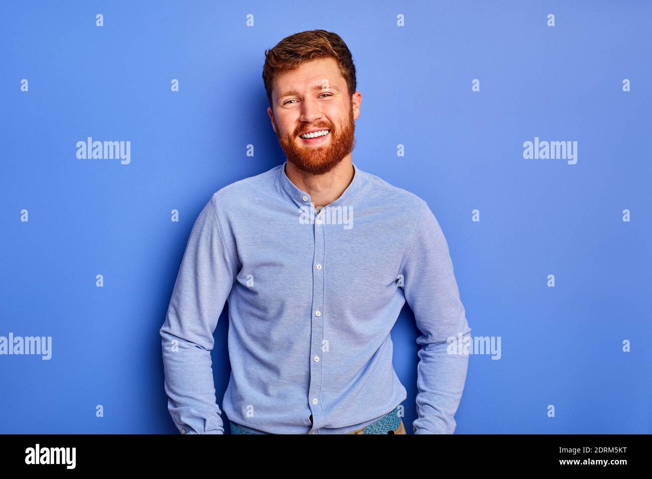 positive guy smiles at camera isolated on blue studio background ...