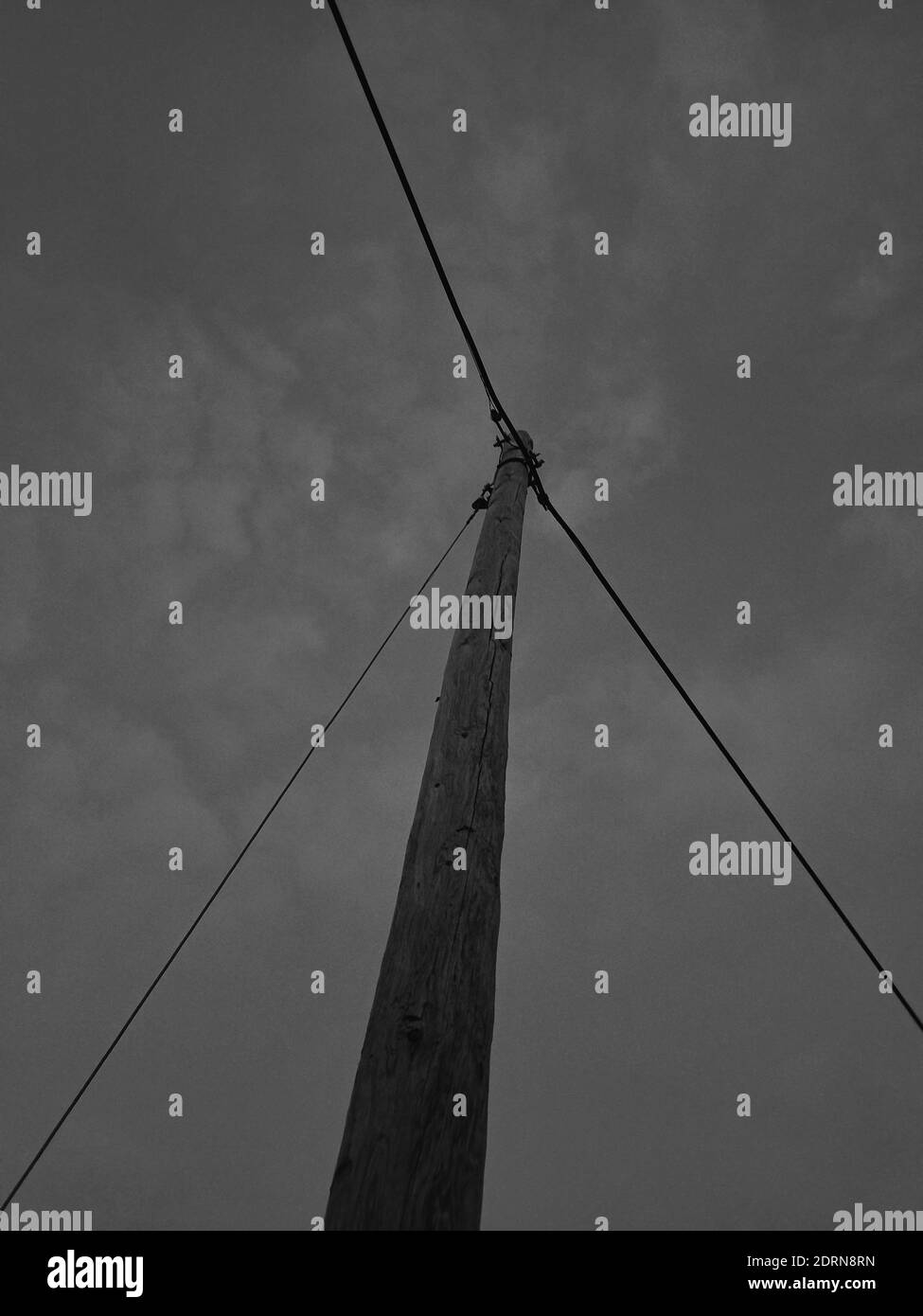 A vertical black-white shot of a wooden power pole on the cloudy sky ...