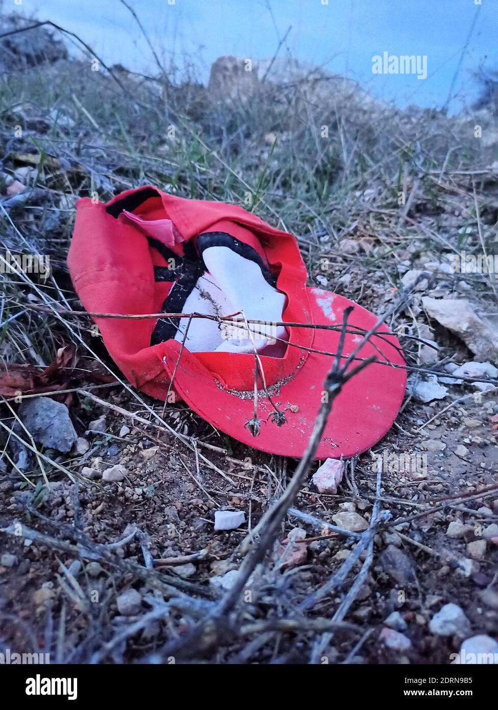 A vertical shot of red-colored old dirty cap laying on the ground ...