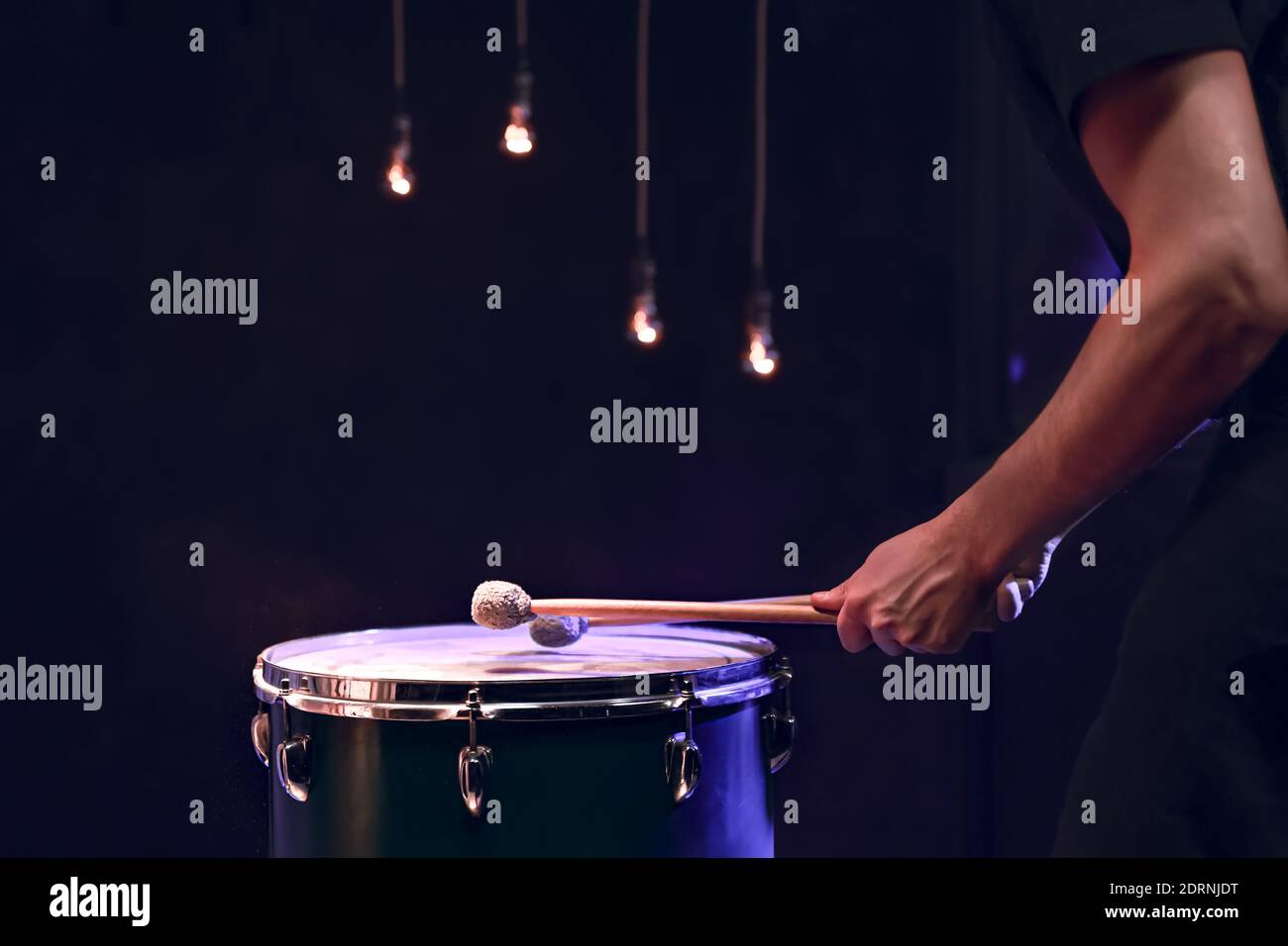 The percussionist plays with sticks on the floor tom in a dark room ...