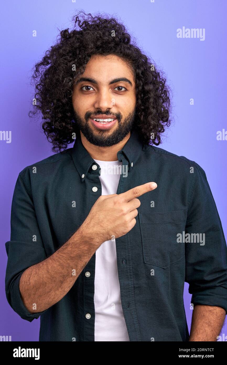 portrait of curly arabic man pointing finger at side, index at right ...